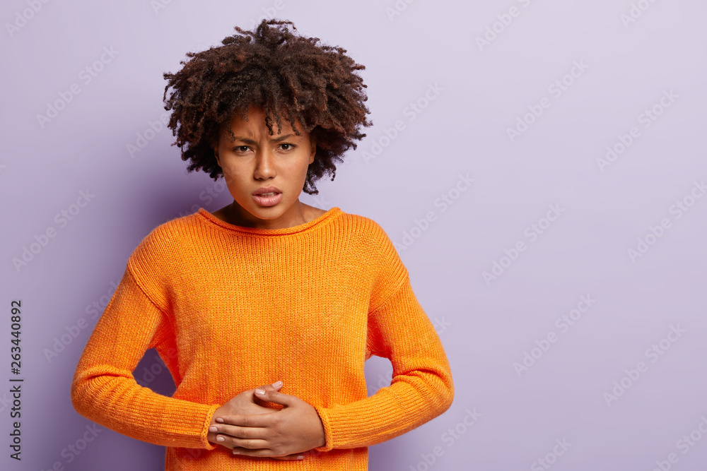 Dissatisfied dark skinned female keeps hands on stomach, suffers from ...