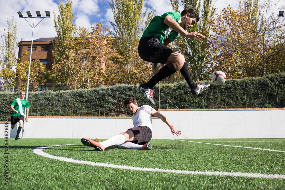 Determined football player kicking ball on field overjumping player on ...