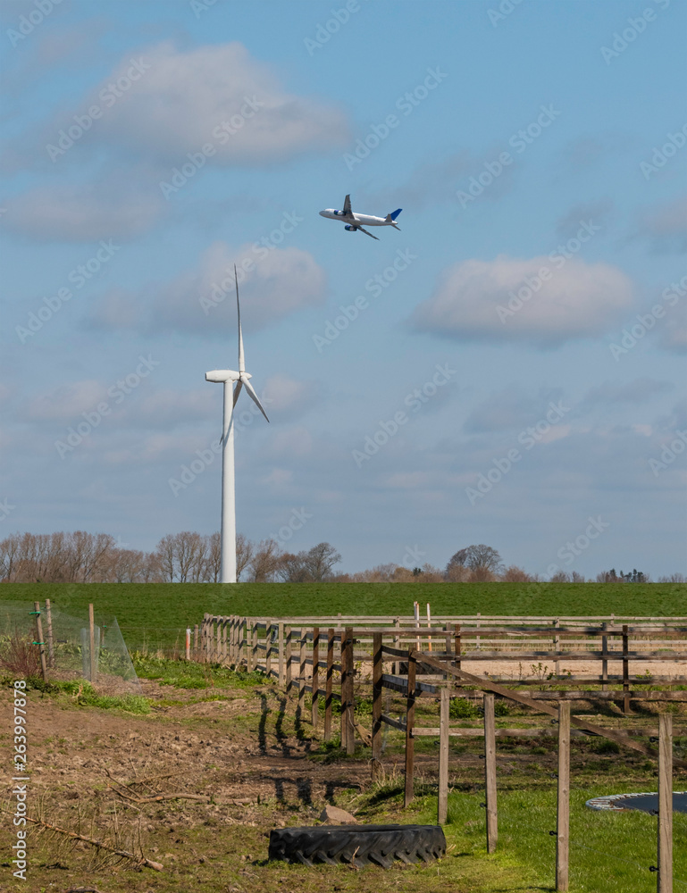 Aircraft flying close to a wind turbine standing in a field in Denmark ...