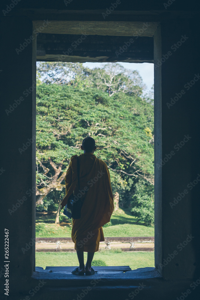 Back view of monk standing in arch of ancient temple and looking at ...
