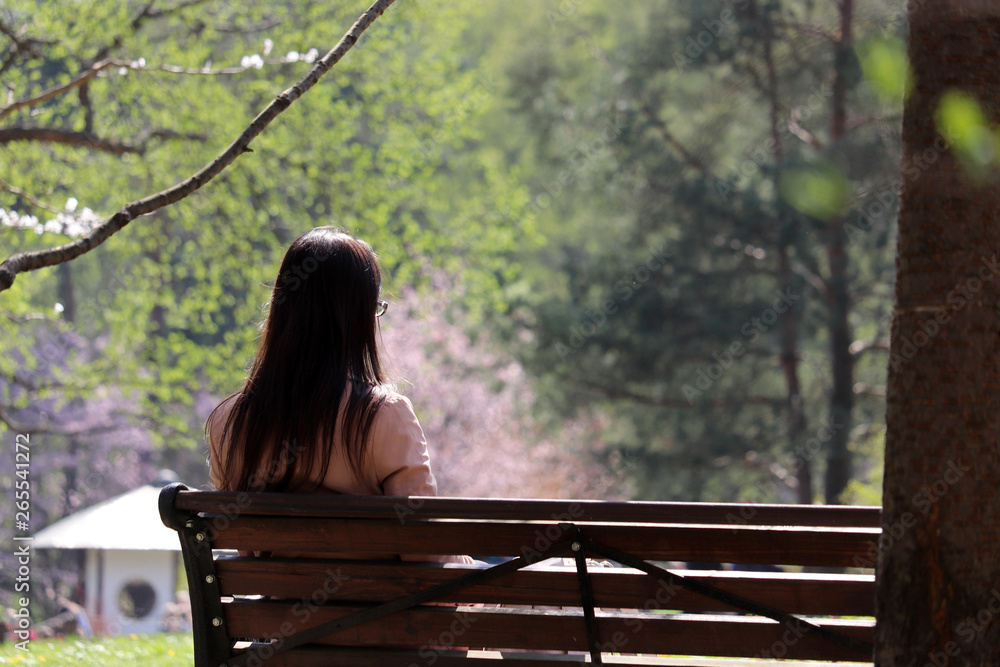 Girl in glasses sits on a wooden bench in a spring japanese garden ...