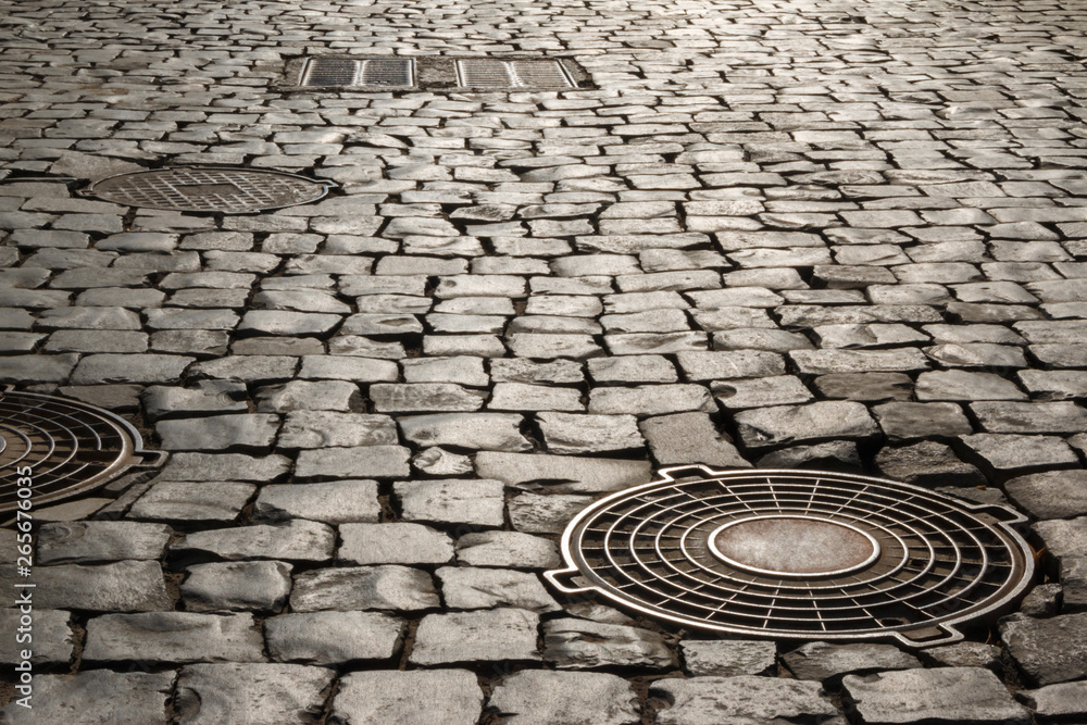 the sunlight on cobblestone road with manhole covers. old paving stone ...