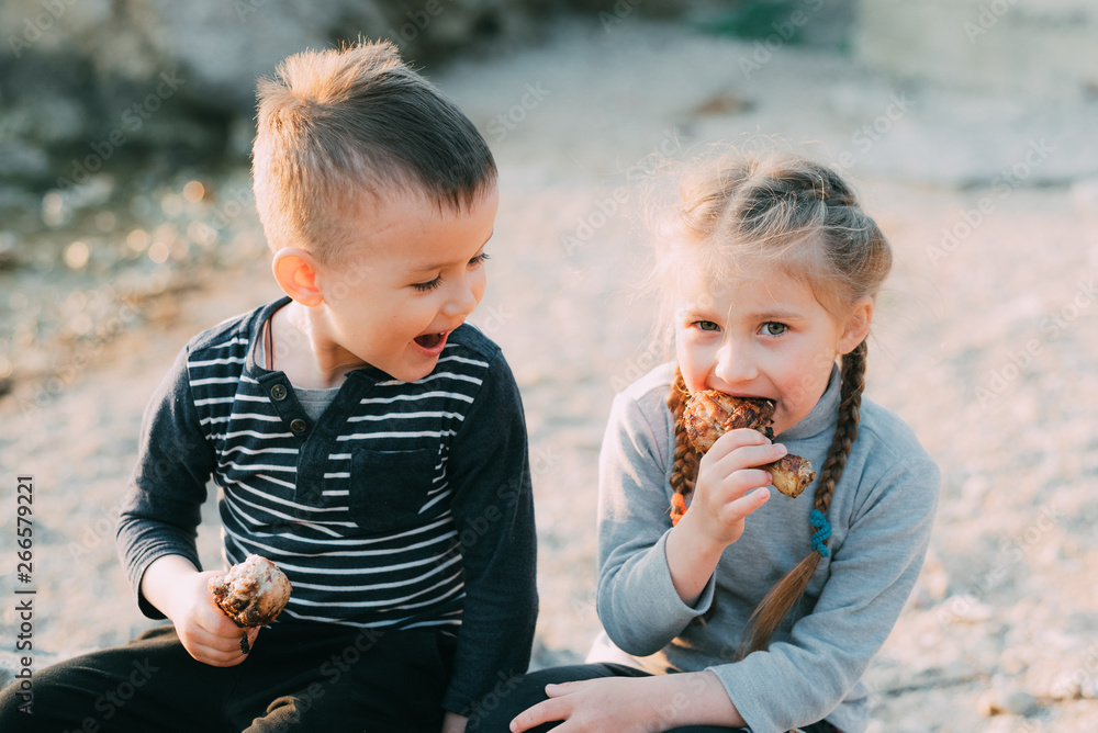 Kids brother and sister have fun eating chicken Shin on the beach near ...