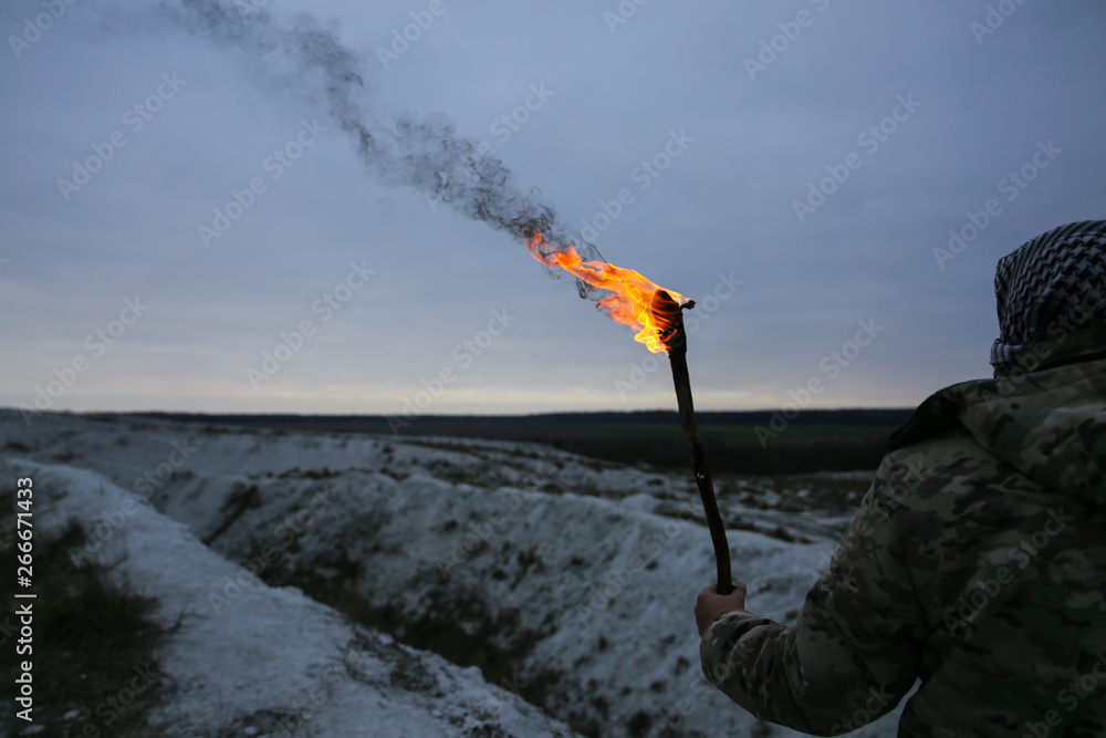 Soldier is holding torch with fire. Man in camouflage uniform and ...