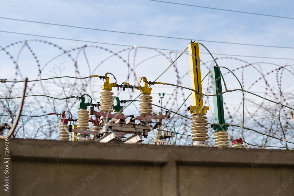 insulators of high voltage transformer behind a fence with barbed wire ...