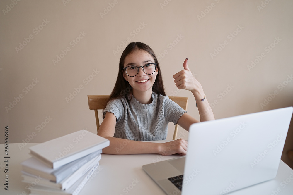 Cute teenager girl doing homework sitting behind the table at home ...