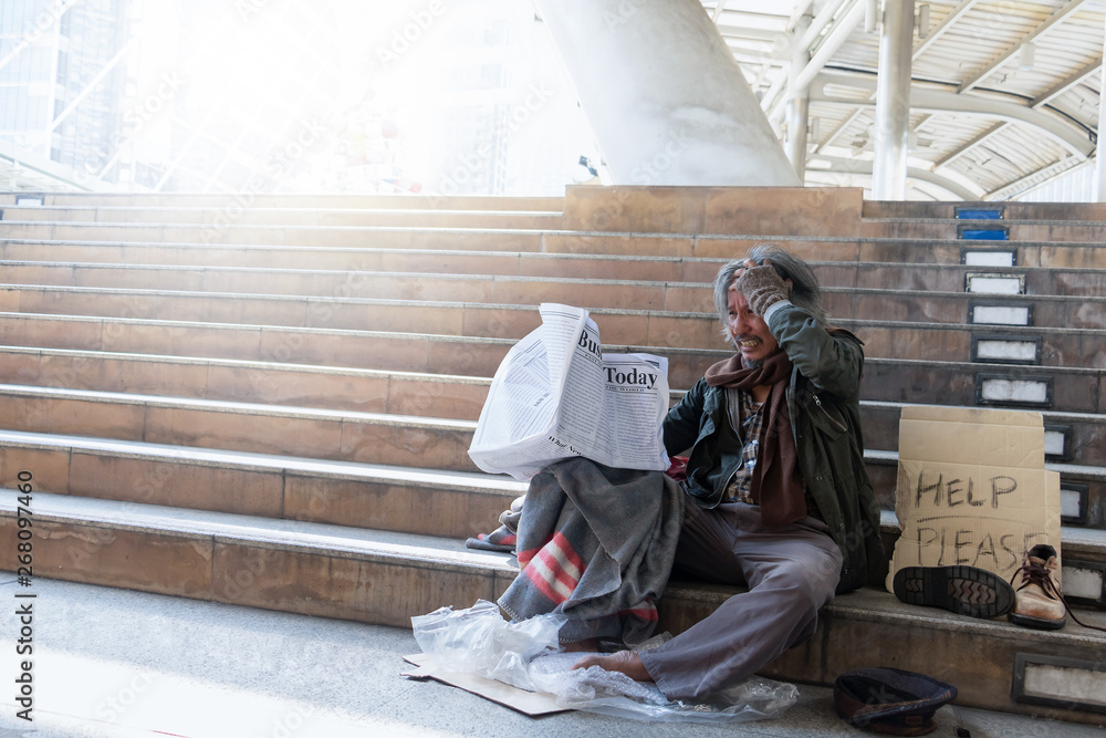 Homeless man is sitting down on staircase in town.He is read newspaper ...