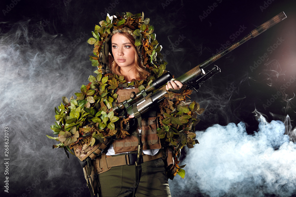 Heavily armed female soldier in battle helmet and ghillie suit holding ...