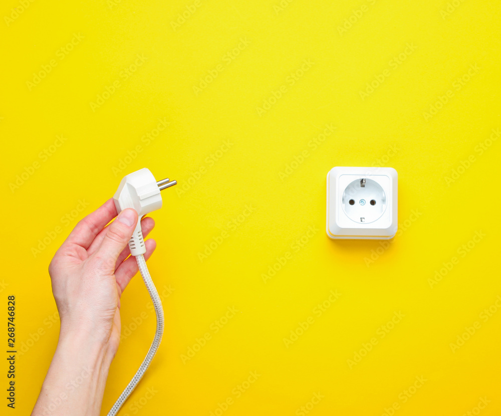 Female hands plug in power plug into electro outlet on yellow ...
