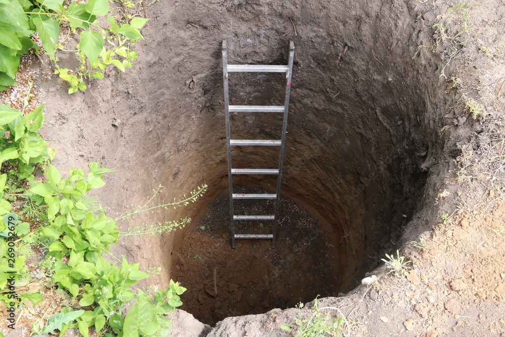 Deep pit in the ground. In the pit shovel and ladder. Digging a hole ...