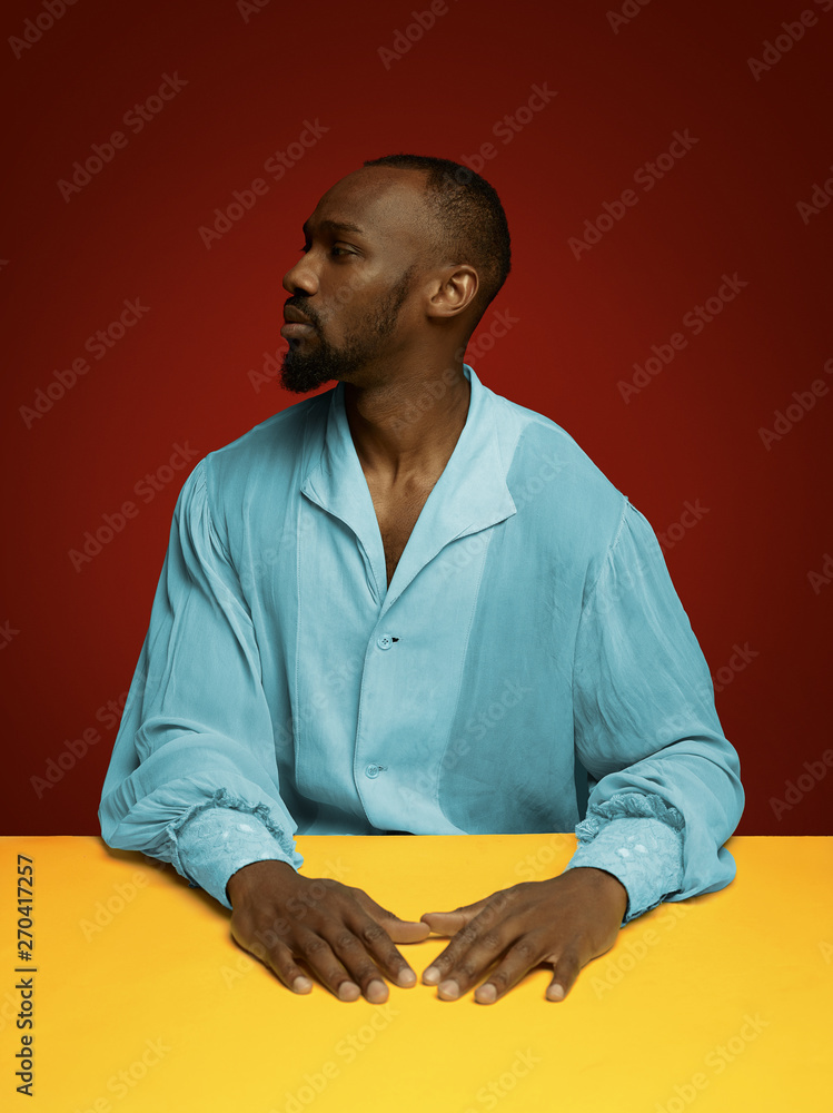 Young man as a medieval grandee or nobleman on red studio background ...