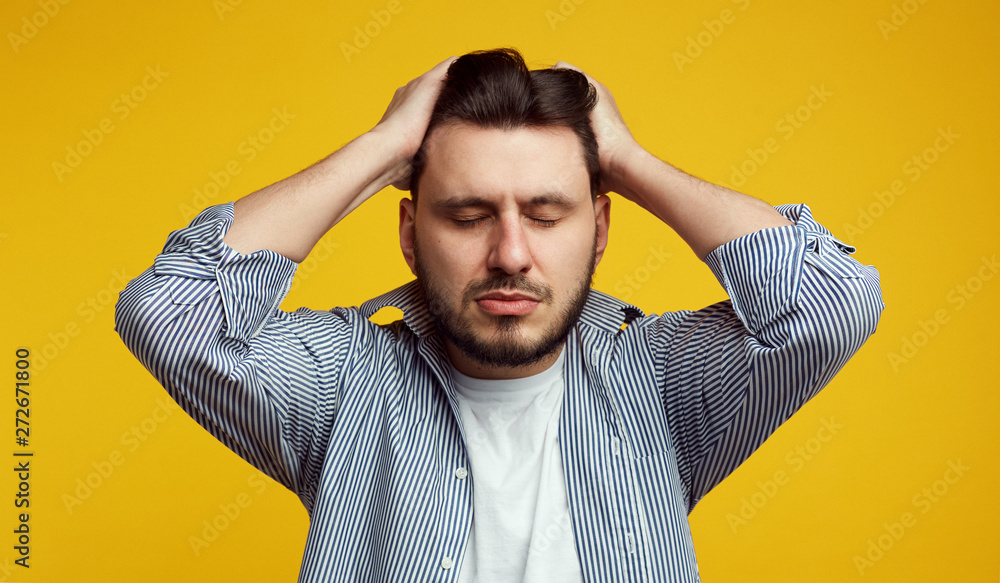 Upset young man keeps both hands on head, closes eyes, suffers from ...