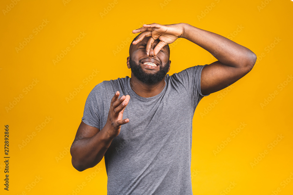 Afro american man isolated against yellow background smelling something ...