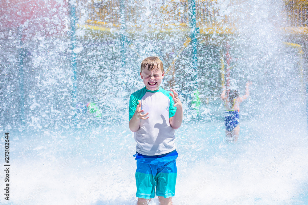 Young boy getting soaking wet while at an outdoor water park. Lots of ...
