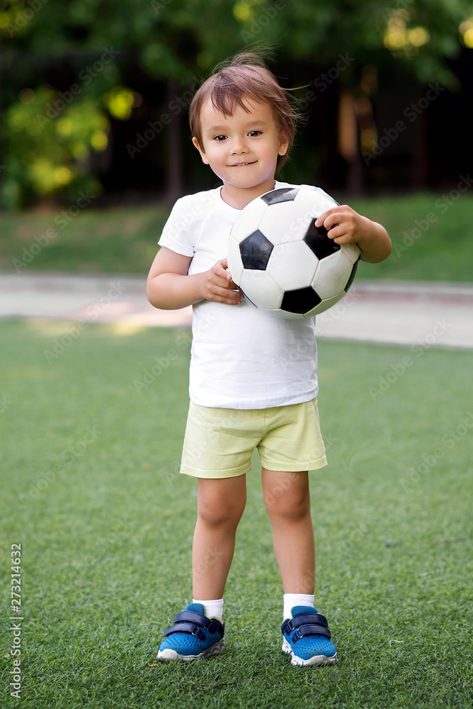 Portrait of little toddler child standing in green football field ...