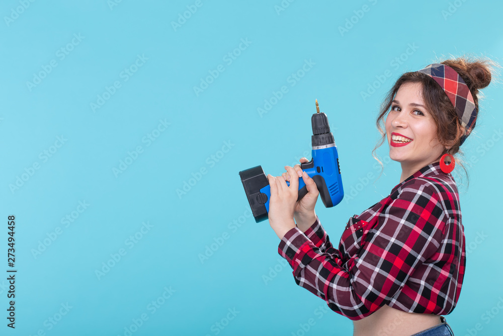 Sexy young pin-up woman with drill over blue background with copy space ...