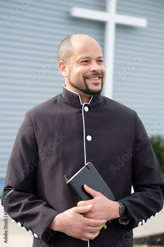 A african-american Male Reverend stands in front of a church with a ...