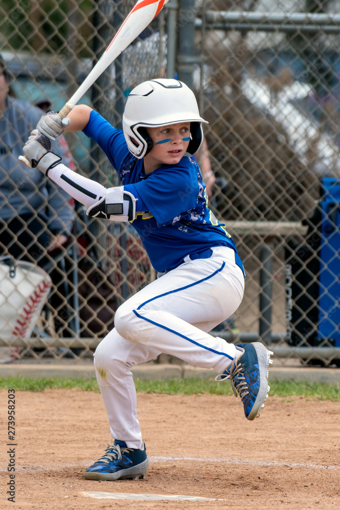 Youth baseball player in blue uniform and white helmet lifts leg in ...