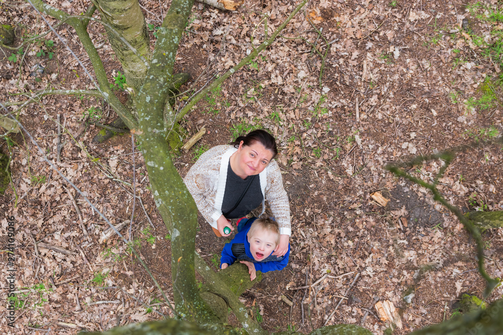 Top view of mother and son with down syndrome looking up at a tall tree ...