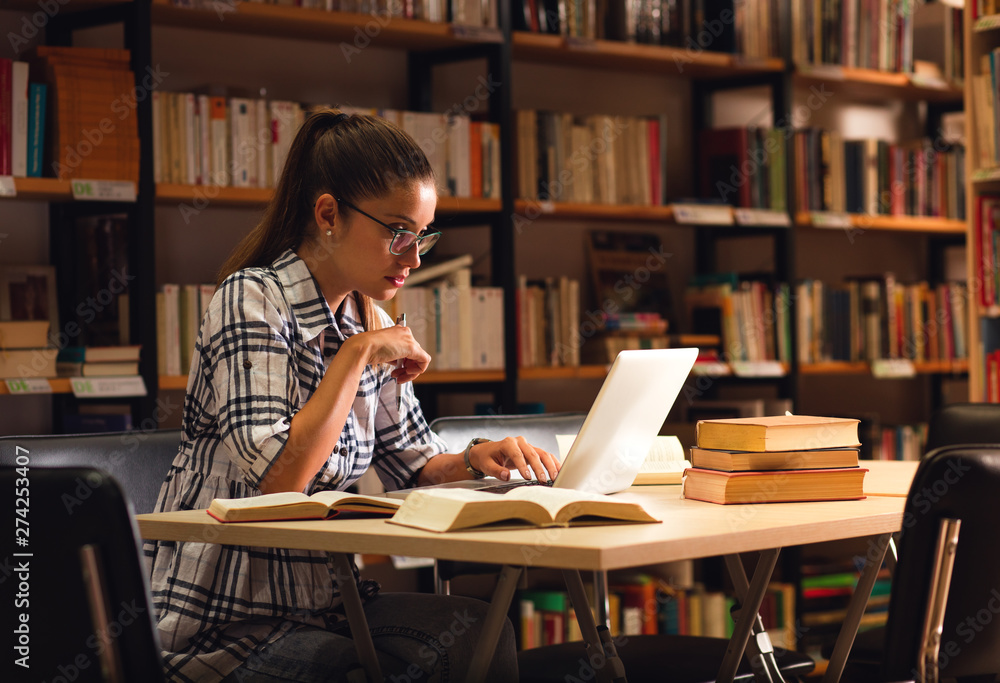 Young female student study in the library using laptop for researching ...