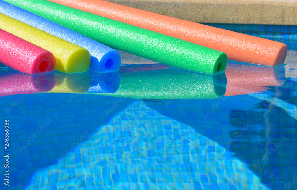 Brightly coloured pool noodles floating in a swimming pool, with ...