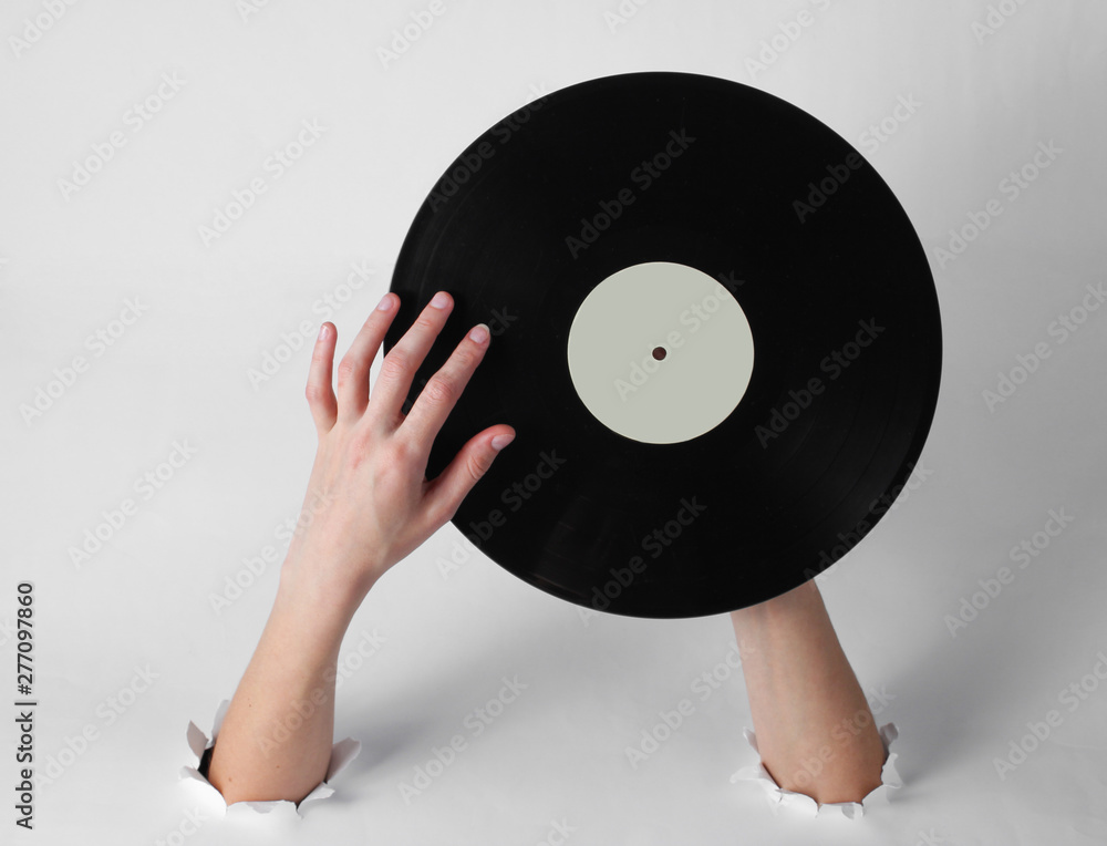Female hands rotates a vinyl record through the torn holes of a white ...