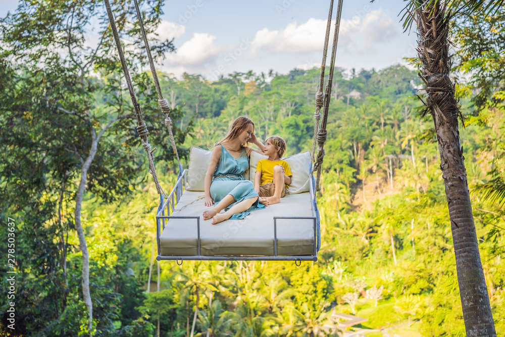 Mother and son swinging in the jungle rainforest of Bali island ...
