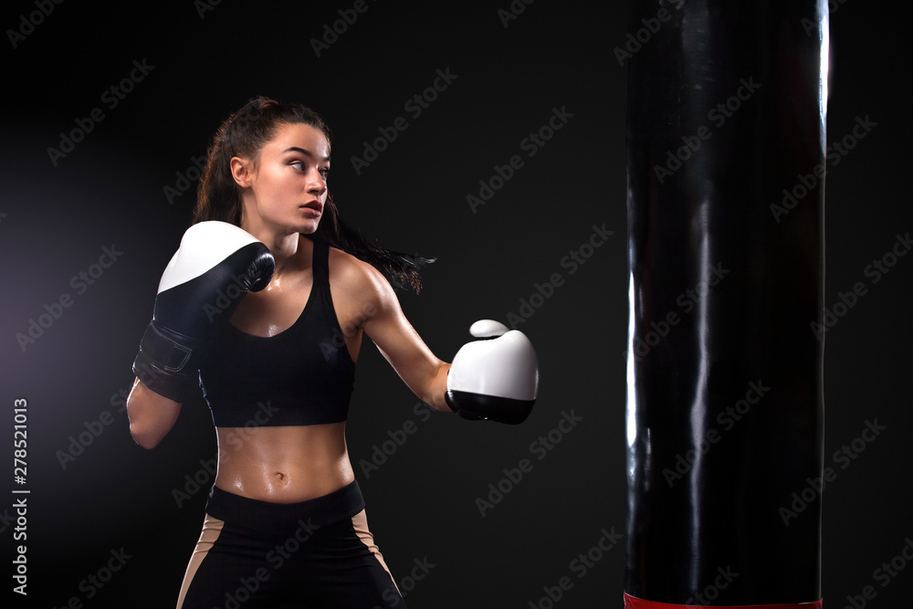 Woman boxer fighting in gloves with boxing punching bag on black ...