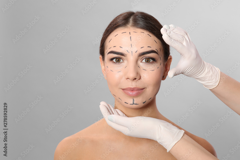 Doctor examining woman's face with marker lines for plastic surgery ...