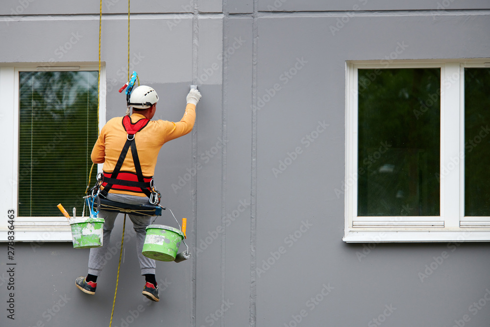 Photo Stock Worker hanging on rope and paints building wall with roller ...