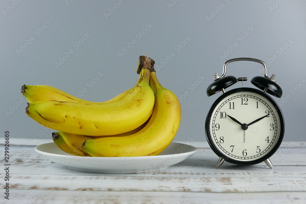 Selective focus bunch of bananas and alarm table clock show 10 past 10 ...