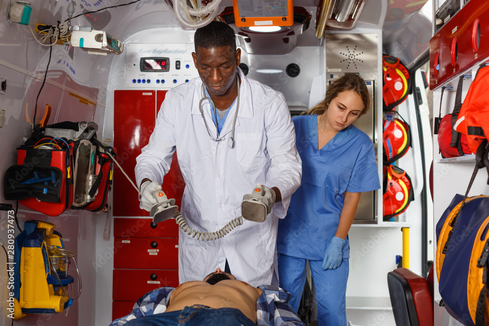 Emergency doctor resuscitating male patient with help of defibrillator ...