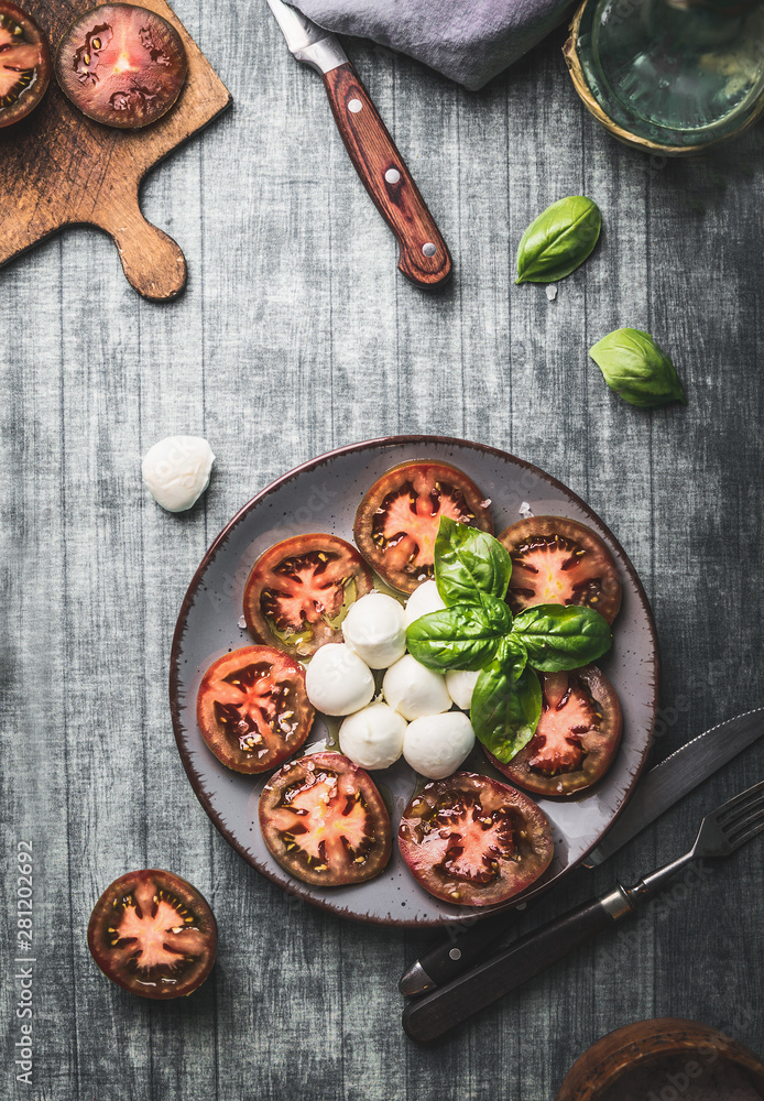 Tomatoes mozzarella balls salad with basil leaves on rustic table with ...
