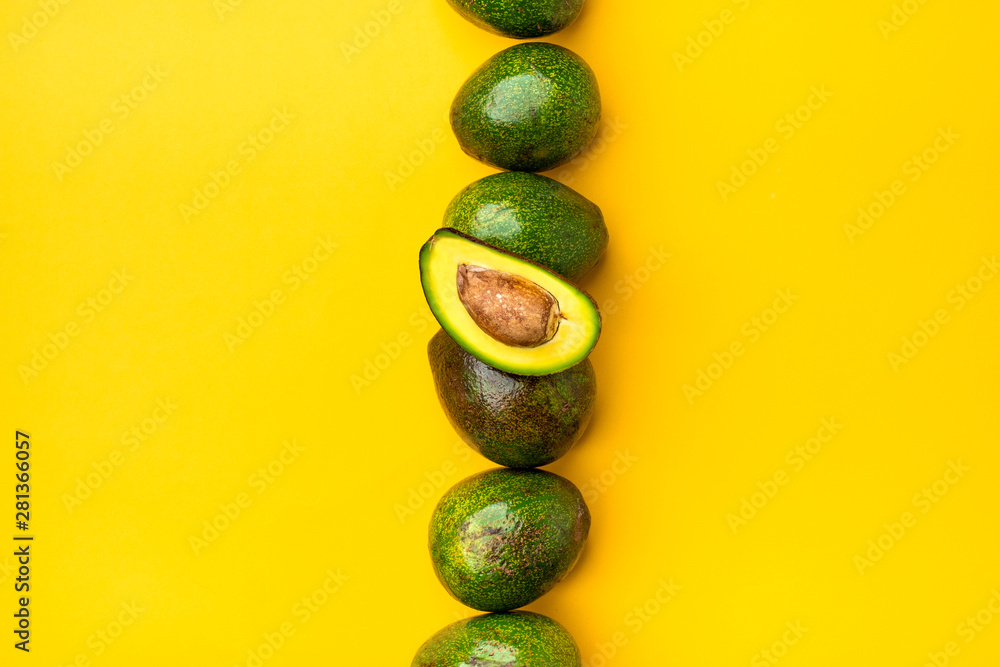 organic avocados half cut with seed and whole fruit on yellow table ...