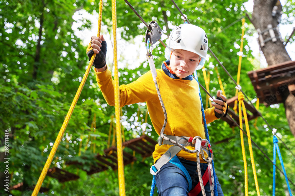 young boy in helmet in the rope park pass obstacles route high among ...
