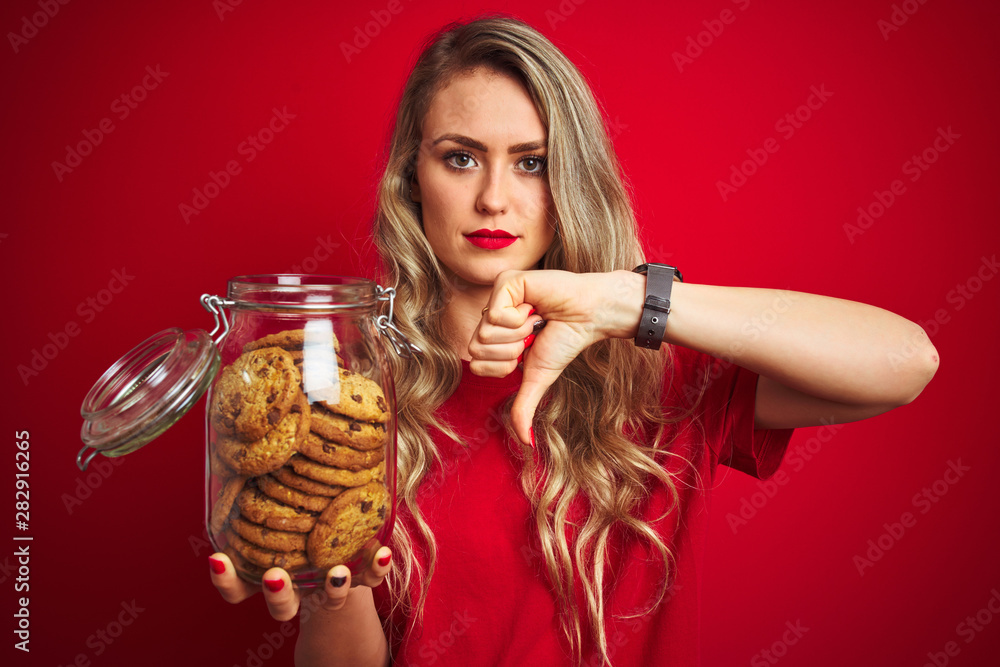 Young beautiful woman holding a jar of cookies over red isolated ...