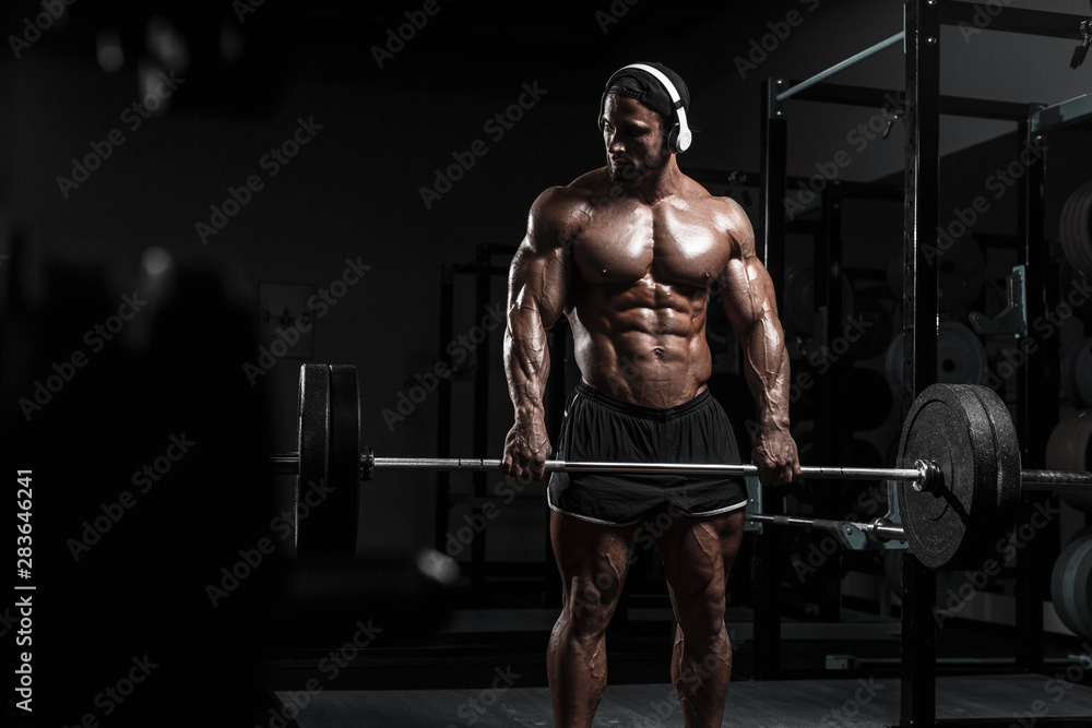 Muscular athletic bodybuilder man hard training in gym over dark ...