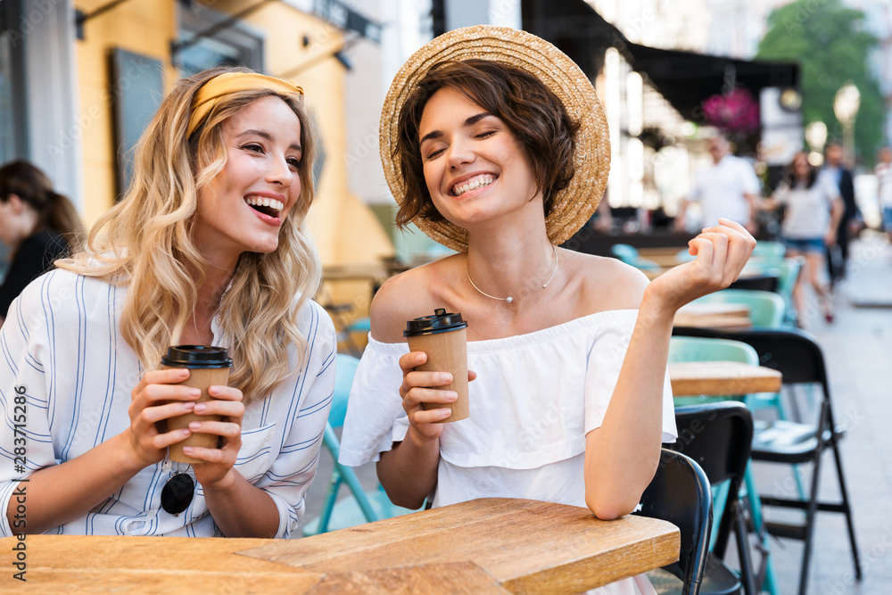 Happy young positive optimistic girls friends sitting outdoors in cafe ...