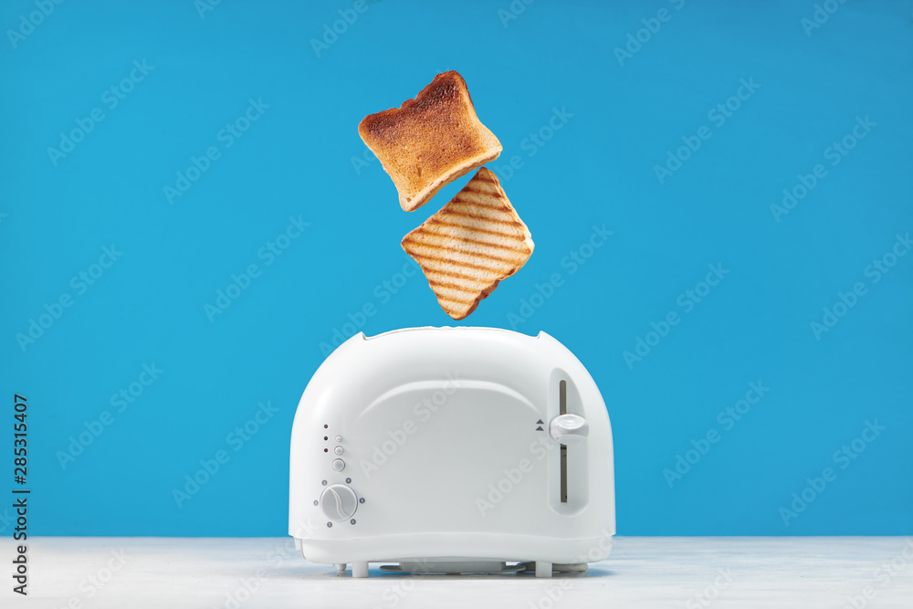 Roasted toast bread popping up of toaster with blue wall, front view ...