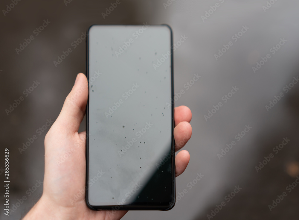 smartphone in hand in the rain on the street. frameless Bezel-less ...
