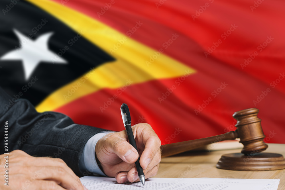 Judge writing on paper in courtroom with East Timor flag background ...