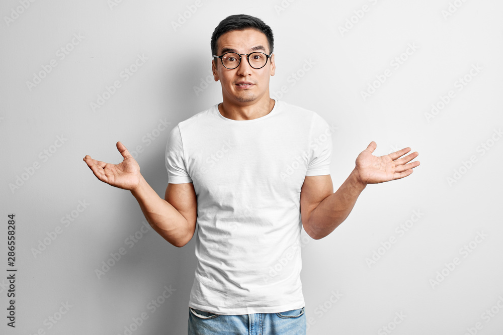 Foto de Stock Puzzled Asian man dressed in casual and glasses with arms ...