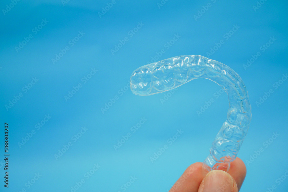 hand holding clear plastic retainer teeth that isolated on blue sky ...