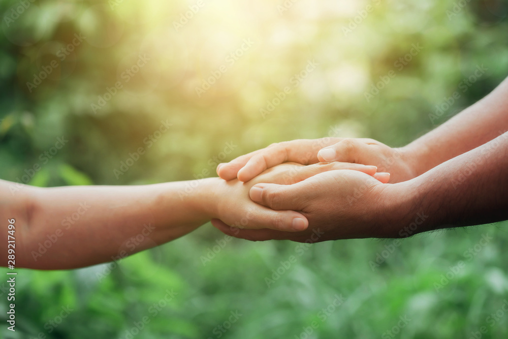 Close up of Two people holding hand together over blurred green nature ...