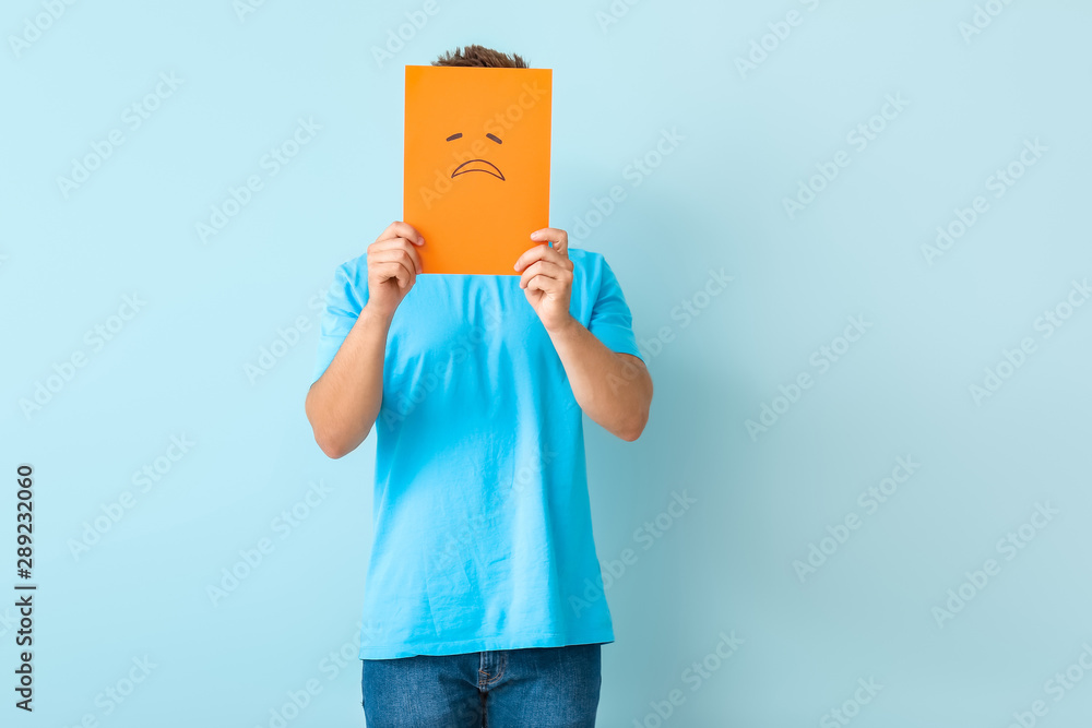 Young man hiding face behind emoticon against color background Stock ...