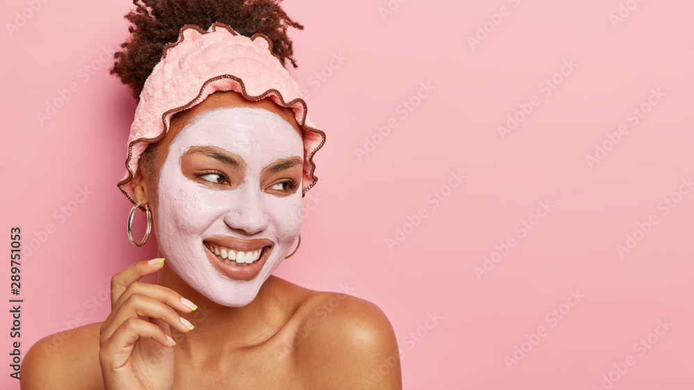 Smiling charming young woman cares about skin, applies clay mask ...