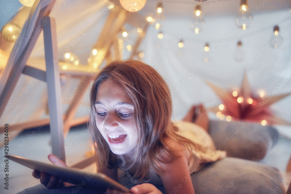 Little 10 year old girl using tablet under her home-made tent inside ...