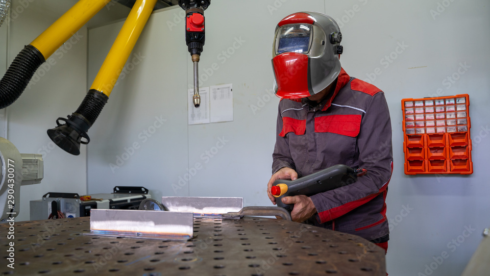 Engineers use a wireless remote control of robotic welding and robot ...