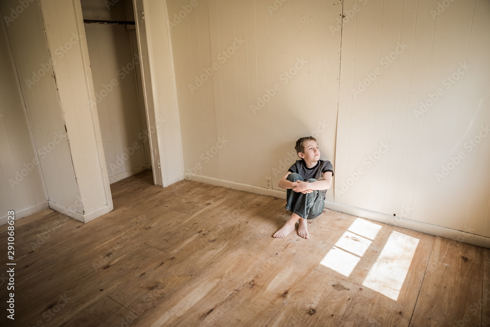 Boy sitting alone in an empty room looking out the window Stock Photo ...