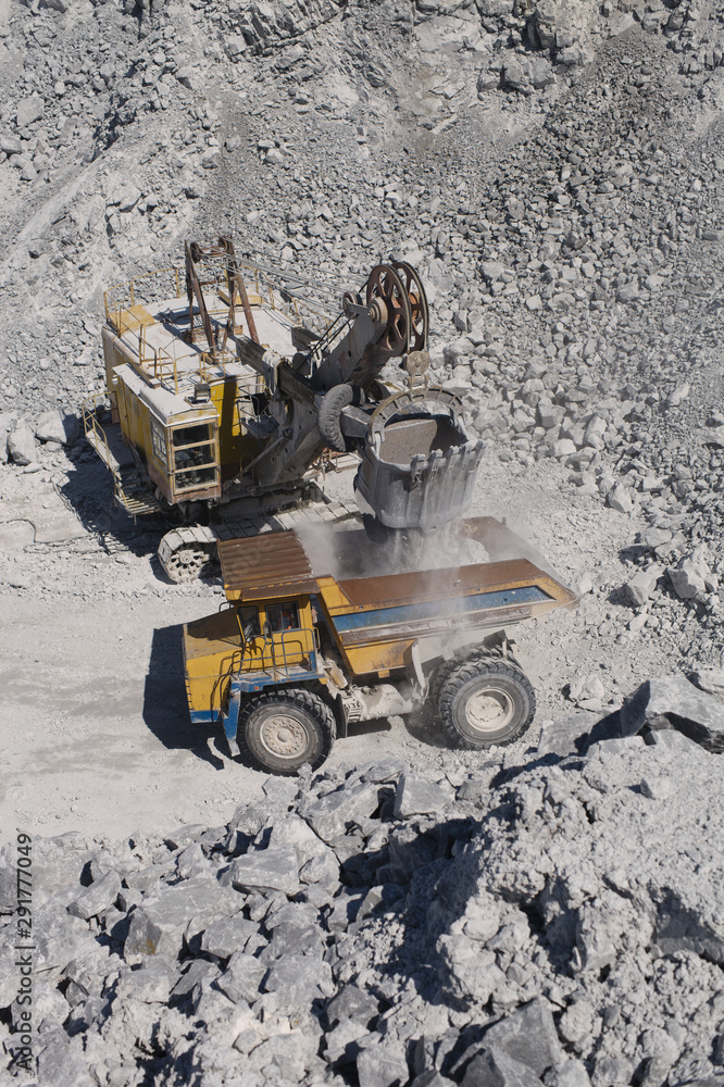 Heavy mining excavator loads rock ore into a heavy dump truck in a ...